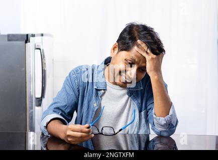 An Indian male with spectacles facing headache sitting beside a table ...