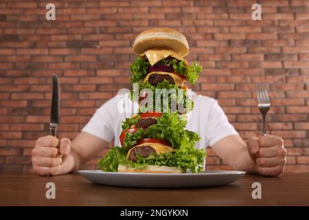 Hungry man with cutlery and huge burger at white table on yellow ...