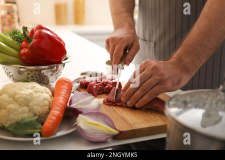 Man cutting meat to make bouillon in kitchen, closeup. Homemade recipe ...