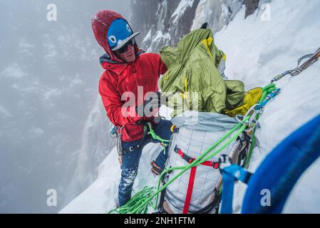 Ice climber putting on heavy jacket while on a climb Stock Photo - Alamy