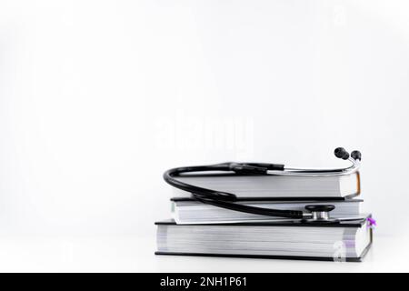 Stethoscope listening to stacked medicine books. White background with ...