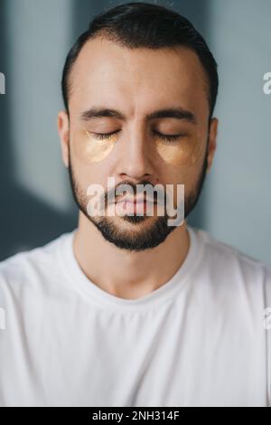 portrait of bearded man with moisturizing eye patches isolated on grey ...