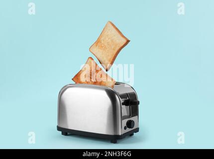 Bread slices popping up from modern toaster on light blue background ...