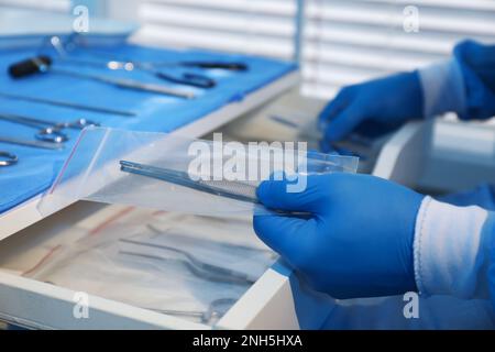 Doctor putting medical forceps into drawer indoors, closeup. Table with ...