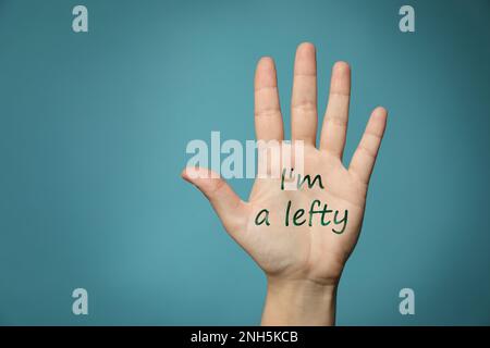 Left-handed woman holding open palm on light blue background, closeup ...