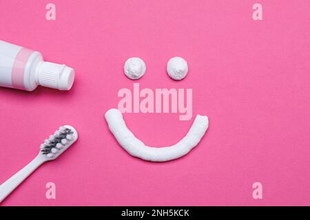 Funny face made with toothpaste and brush on pink background, flat lay ...
