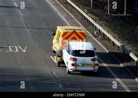 AA rescue vehicle or van towing a broken down car on a trailer along ...