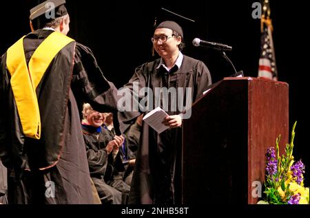 A professor and his students in graduation gowns stand with their arms ...