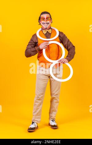 Happy juggler man in makeup vest juggling maces on a yellow background ...