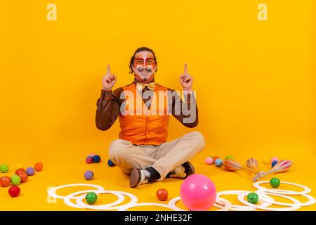 Juggler in waistcoat and with painted face sitting with the juggling ...