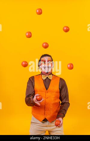 Juggler in a vest and with painted face juggling clubs on a pink ...