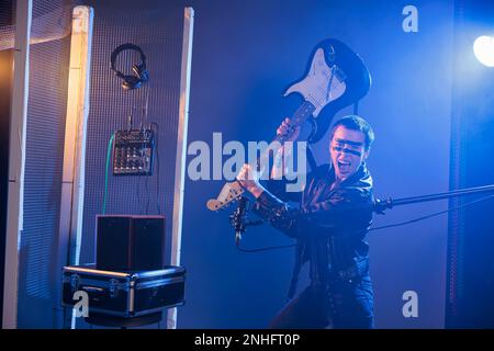 Crazy funky rocker throwing guitar in studio, wearing leather jacket ...