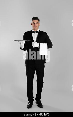 Handsome butler with tray on light grey background, space for text ...