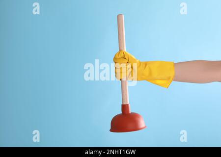 Woman holding plunger on turquoise background, closeup. Space for text ...