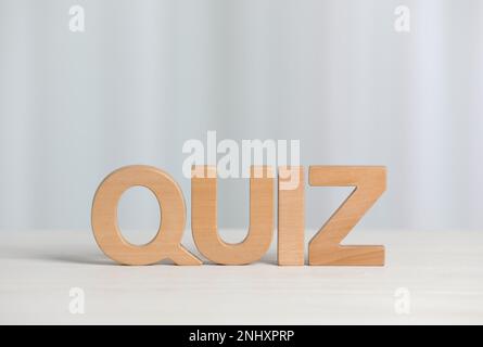 Word Quiz made with wooden letters on table near white brick wall Stock ...