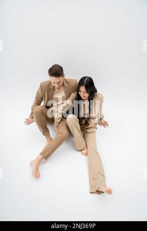full length of cheerful interracial couple sitting near huge template ...