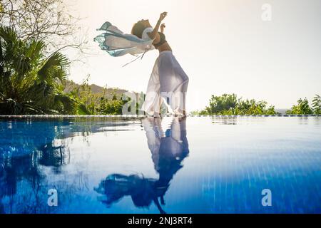Model dancing next to an outdoor tropical pool with the image reflected ...