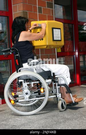 woman in wheelchair throwing mail into a letterbox Stock Photo - Alamy