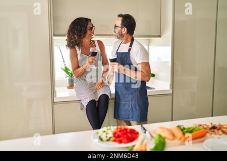 Middle age hispanic couple cook hugging and toasting with wine at ...