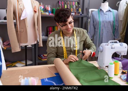 Non binary man tailor smiling confident sitting on table at atelier ...