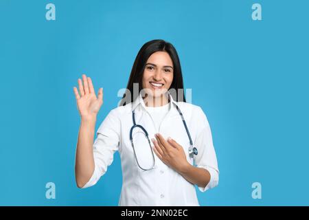 Happy female doctor waving to say hello on light blue background Stock ...