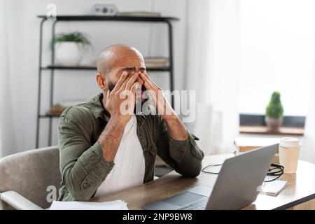 Freelance stress. Tired mature latin man looking at laptop screen and ...