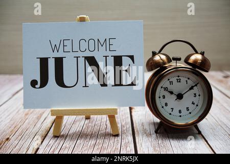 Welcome June text with alarm clock and tulip flower bouquet on marble ...