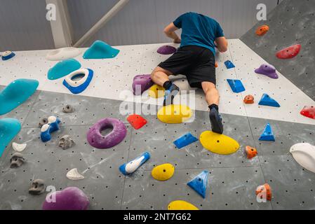 Male climber traversing indoor climbing wall using holds and grips of ...