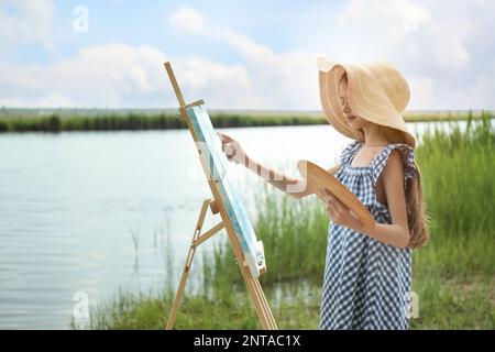 Little girl painting scenery on easel near lake Stock Photo - Alamy