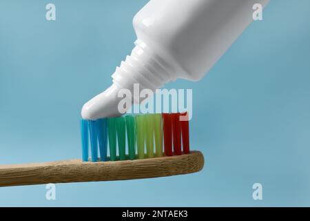 Squeezing toothpaste onto brush against light blue background, closeup ...