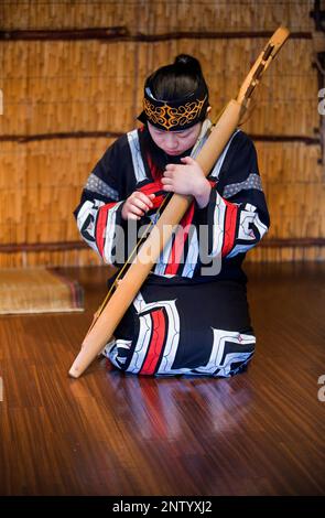 Ainu woman playing a traditional instrument in Ainu village museum ...