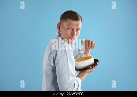 Greedy man hiding tasty cake from woman on turquoise background Stock ...
