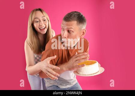 Greedy man hiding tasty cake from woman on pink background Stock Photo ...