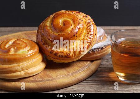 Various sweet buns and transparent cup of tea on wooden table Stock ...
