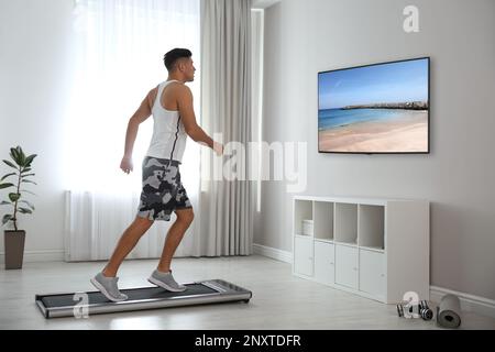 Sporty man training on walking treadmill and watching TV at home Stock ...