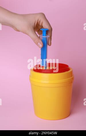 Doctor throwing used syringe needle into sharps container on light blue ...