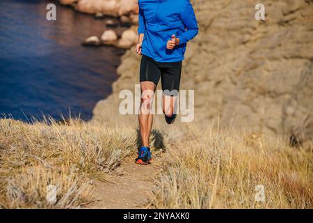 male runner running along seashore trail with dry grass on blue sky ...