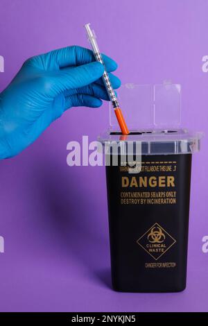 Doctor throwing used syringe into sharps container on light blue ...