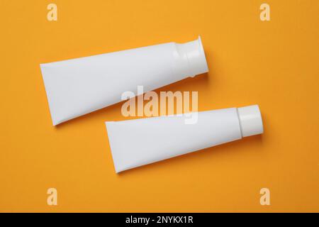 Blank tubes of toothpaste on orange background, flat lay. Space for ...