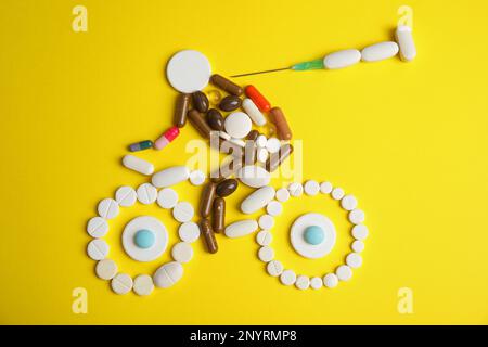 Bike made of pills and syringe on yellow background, flat lay. Using ...