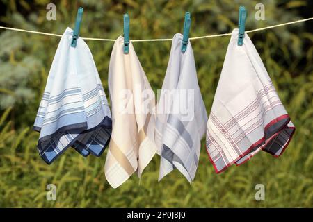 Different handkerchiefs hanging on rope near red brick wall outdoors ...