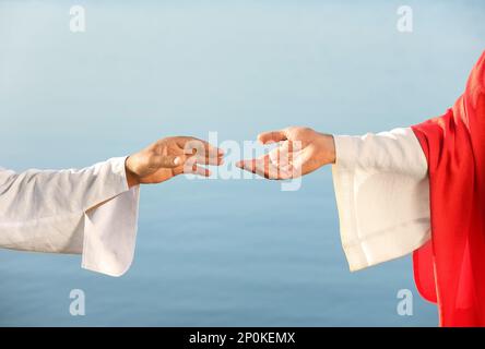 Man reaching for Jesus Christ's hand near water outdoors, closeup Stock ...