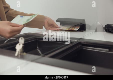 Cashier checking money with currency detector at exchange department ...