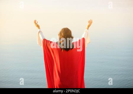 Jesus Christ raising hands near water outdoors, back view Stock Photo ...