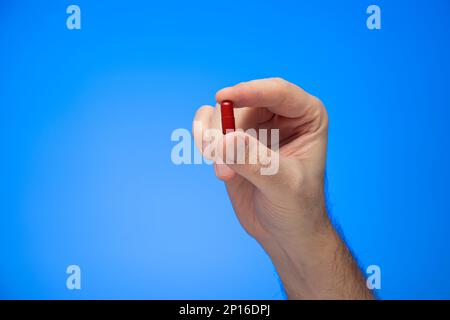 Red medical pill held between fingers by Caucasian male hand isolate on ...