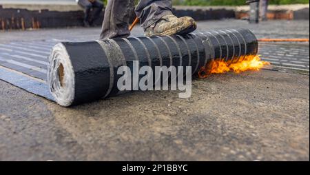 Workers placing a vapor barrier on the roof using a propane gas torch ...