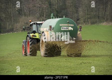 Claas tractor with slurry tanker, spreading slurry on grassland near ...
