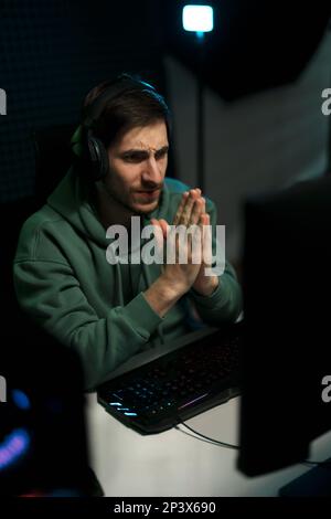 Stressed male cybersport gamer playing video game and praying with hope ...