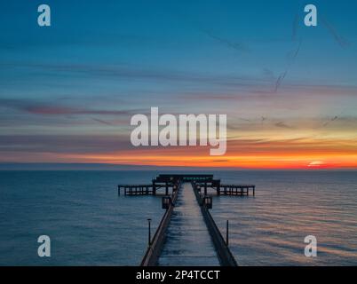 A scenic dock extending out into the glistening ocean at a sunset hour ...