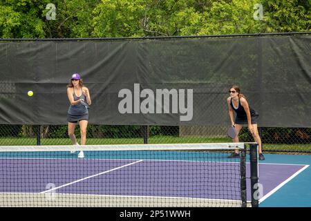 A pickleball player serves the ball as her partner gets ready for a ...